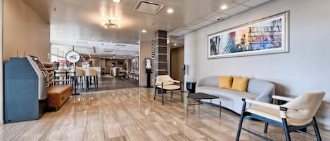 Um hall de hotel moderno com área de estar, balcão de recepção e espaço para refeições.