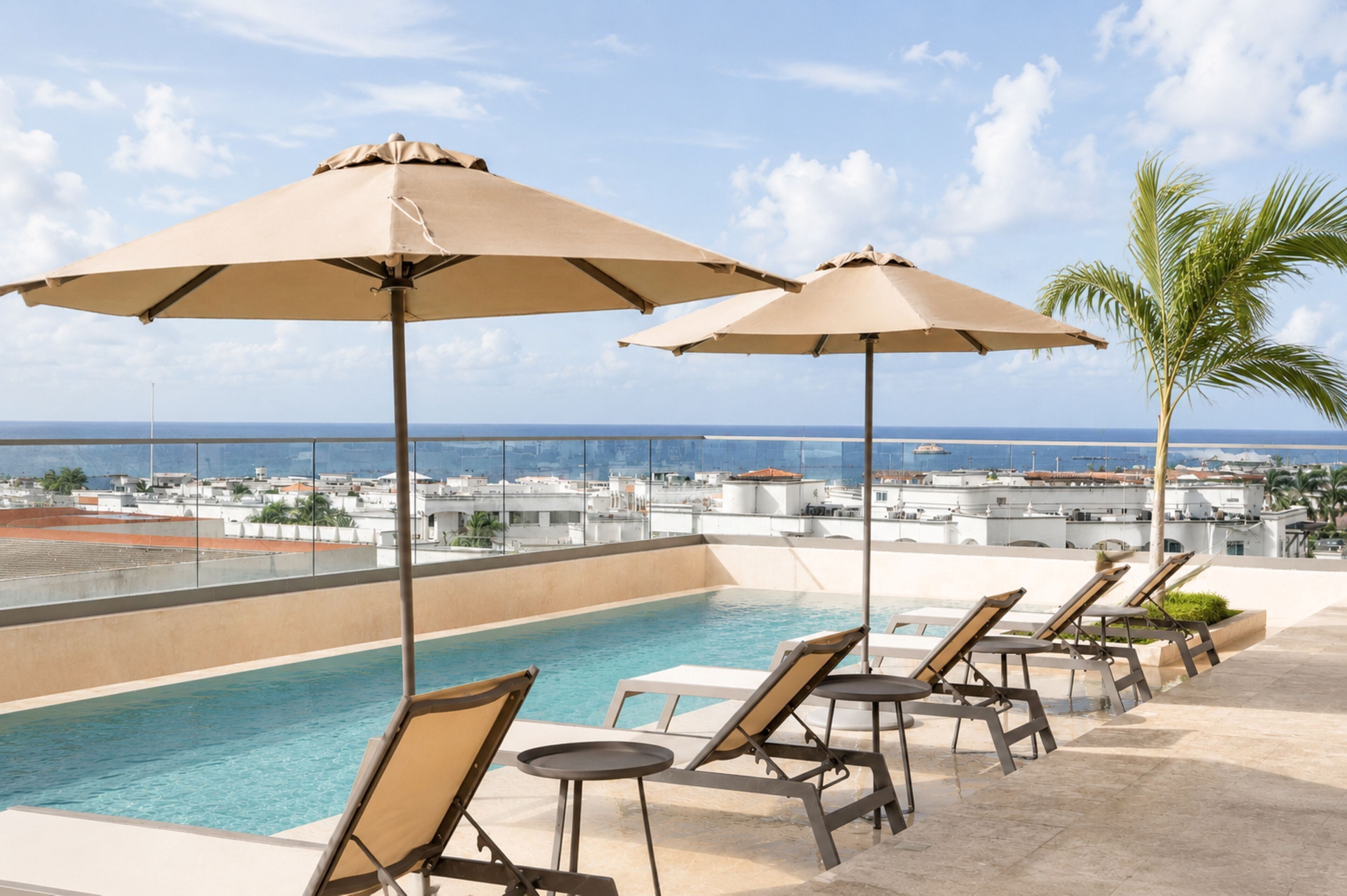 Piscina no terraço com espreguiçadeiras e guarda-sóis, com vista para a paisagem urbana.