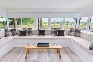 Quarto com área de estar embutida, mesa de madeira e janelas amplas com vista para o exterior.