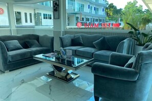 Uma sala de estar moderna com um conjunto de sofá, uma mesa de centro de vidro e vista para um prédio com varandas.