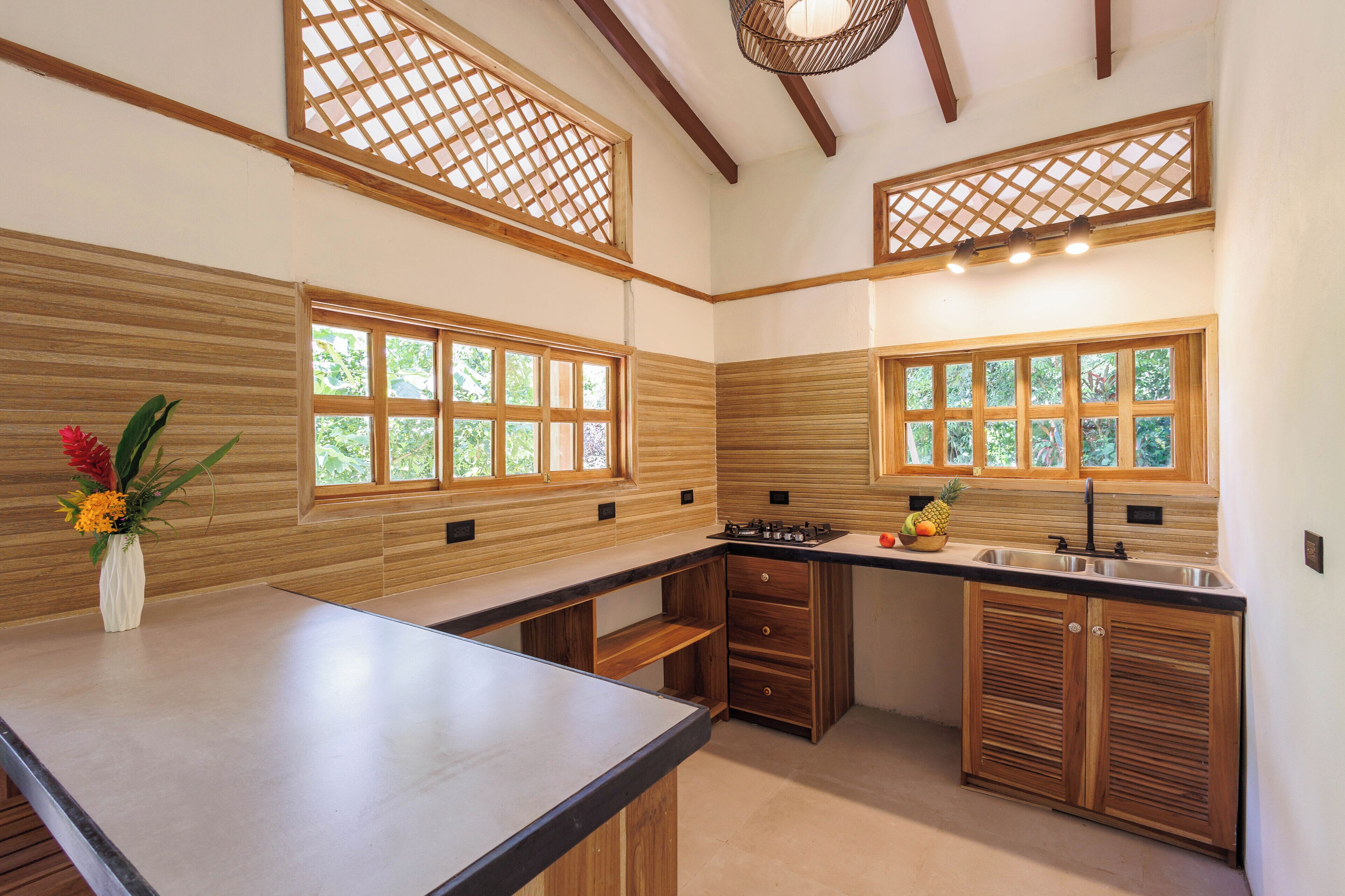 Cozinha moderna com armários de madeira, bancada grande e janela com vista para o verde.