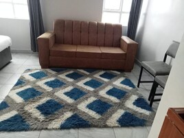 Quarto com sofá marrom, tapete xadrez azul e branco, cadeira cinza e cama com roupa de cama branca.