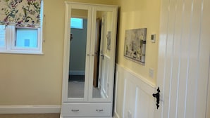 Quarto com um guarda-roupa branco grande, uma janela com cortinas florais e um quadro pendurado na parede.