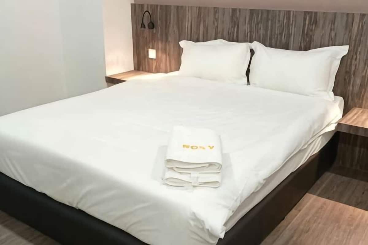 Cama bem arrumada com uma toalha branca dobrada e um travesseiro com a palavra 'ROYAL' bordada.