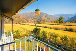 Uma varanda com vista para campos dourados de arroz e montanhas ao fundo.