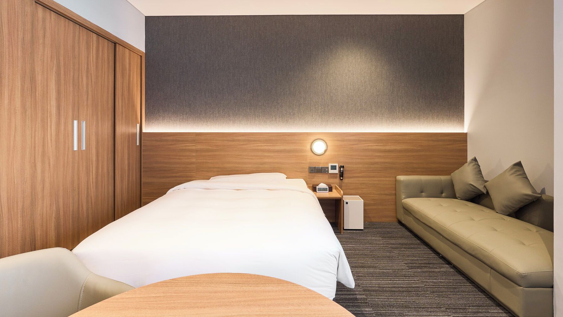 Quarto de hotel com cama, sofá, escrivaninha com luminária e armário.