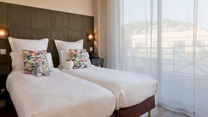 Quarto de hotel com duas camas, uma janela grande e vista para o exterior.