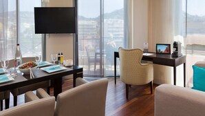 Quarto de hotel moderno com área de jantar, televisão de tela plana, um laptop e varanda com vista.