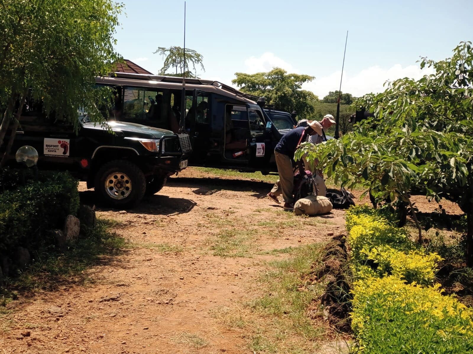 Uma trilha de terra leva a um veículo estacionado em um ambiente rural, com vegetação e árvores.