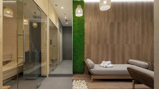 Um spa moderno com chuveiro de vidro, parede verde, piso de madeira, sofá e caminho de pedras.