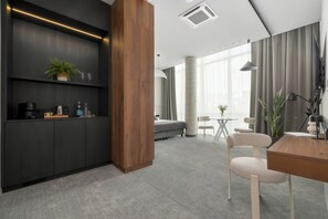 Quarto de hotel moderno com cozinha compacta, janela ampla, cama e área de refeições.