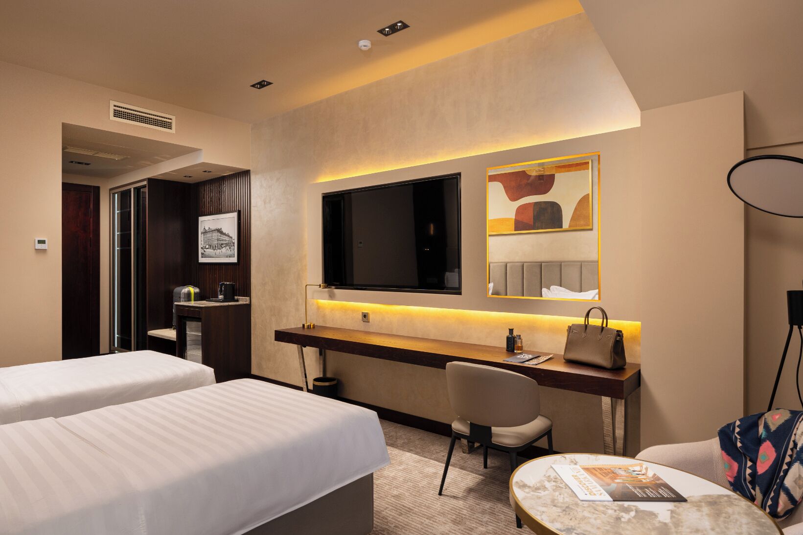 Quarto de hotel com duas camas, uma escrivaninha, uma cadeira, uma televisão e um espelho.