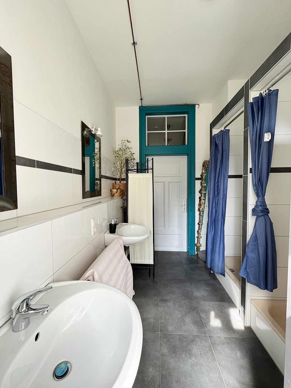 Uma casa de banho moderna com uma grande pia branca, um espelho, uma sanita branca e um chuveiro com cortina azul.