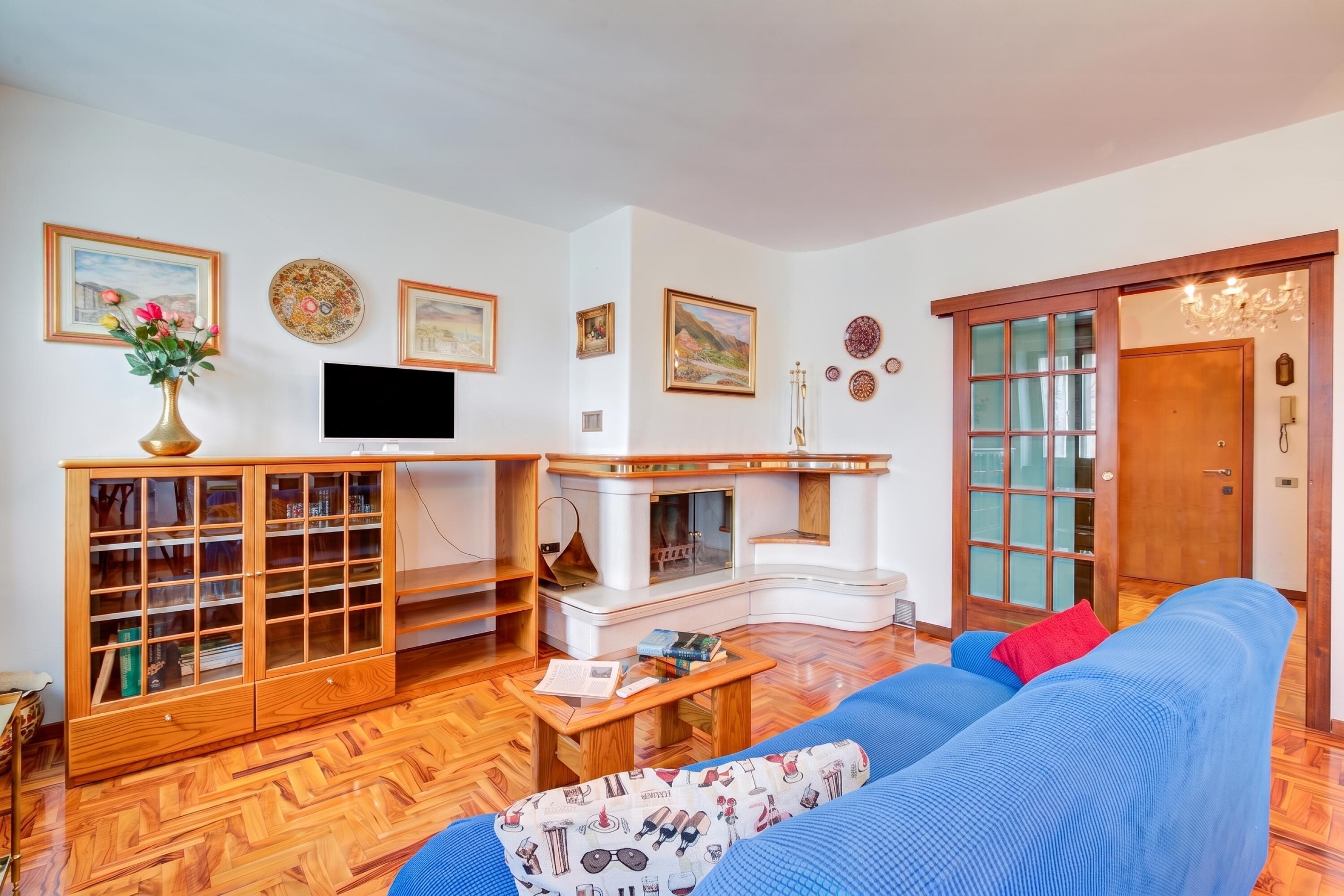 Sala de estar com sofá azul, aparador de madeira, televisão e objetos decorativos na parede.