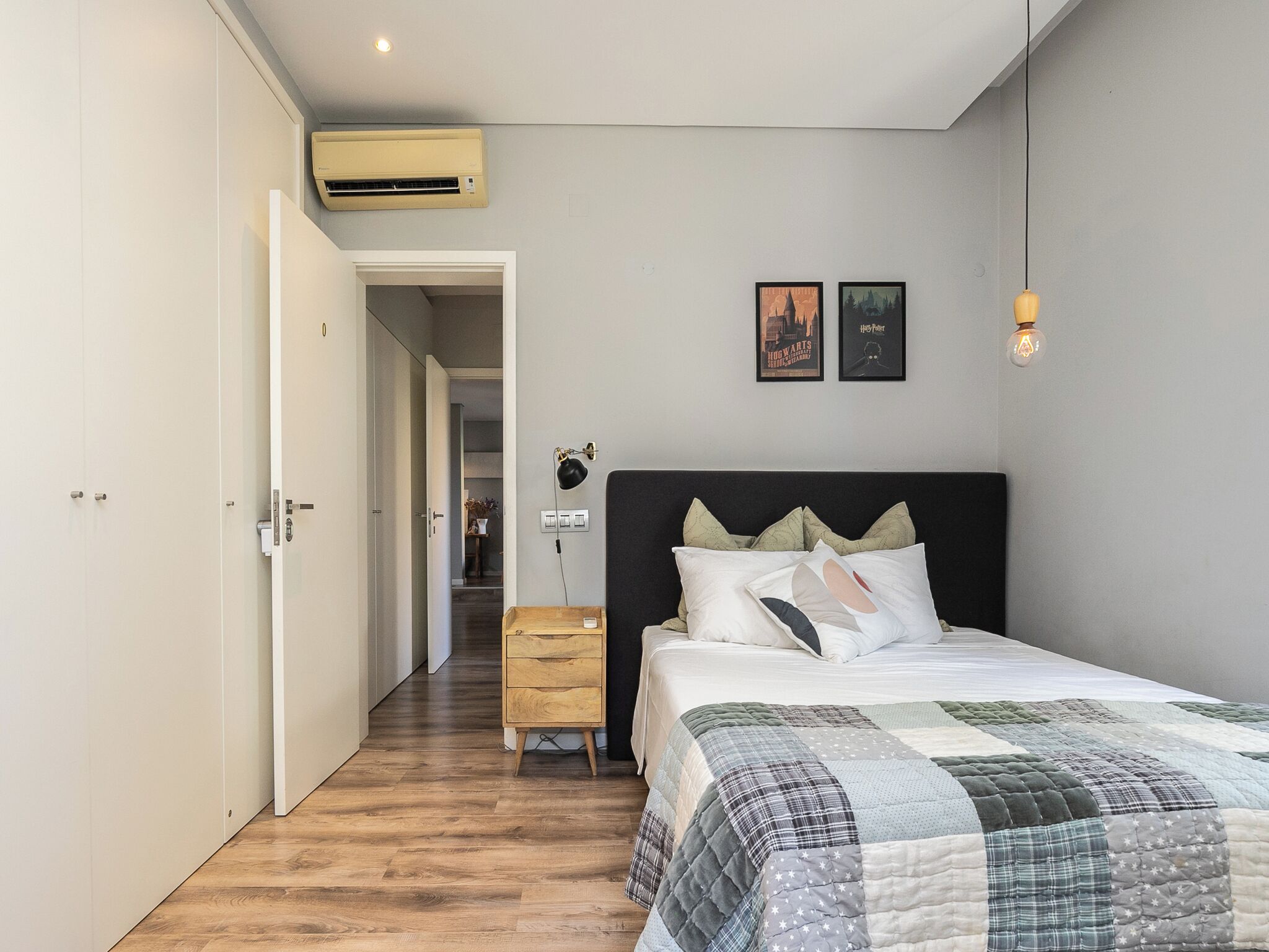 Quarto com cama, mesa de cabeceira, abajur na parede e moldura de quadro.