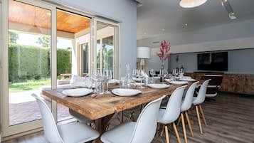Uma área de refeições com uma mesa de madeira posta para seis pessoas, cercada por cadeiras brancas.