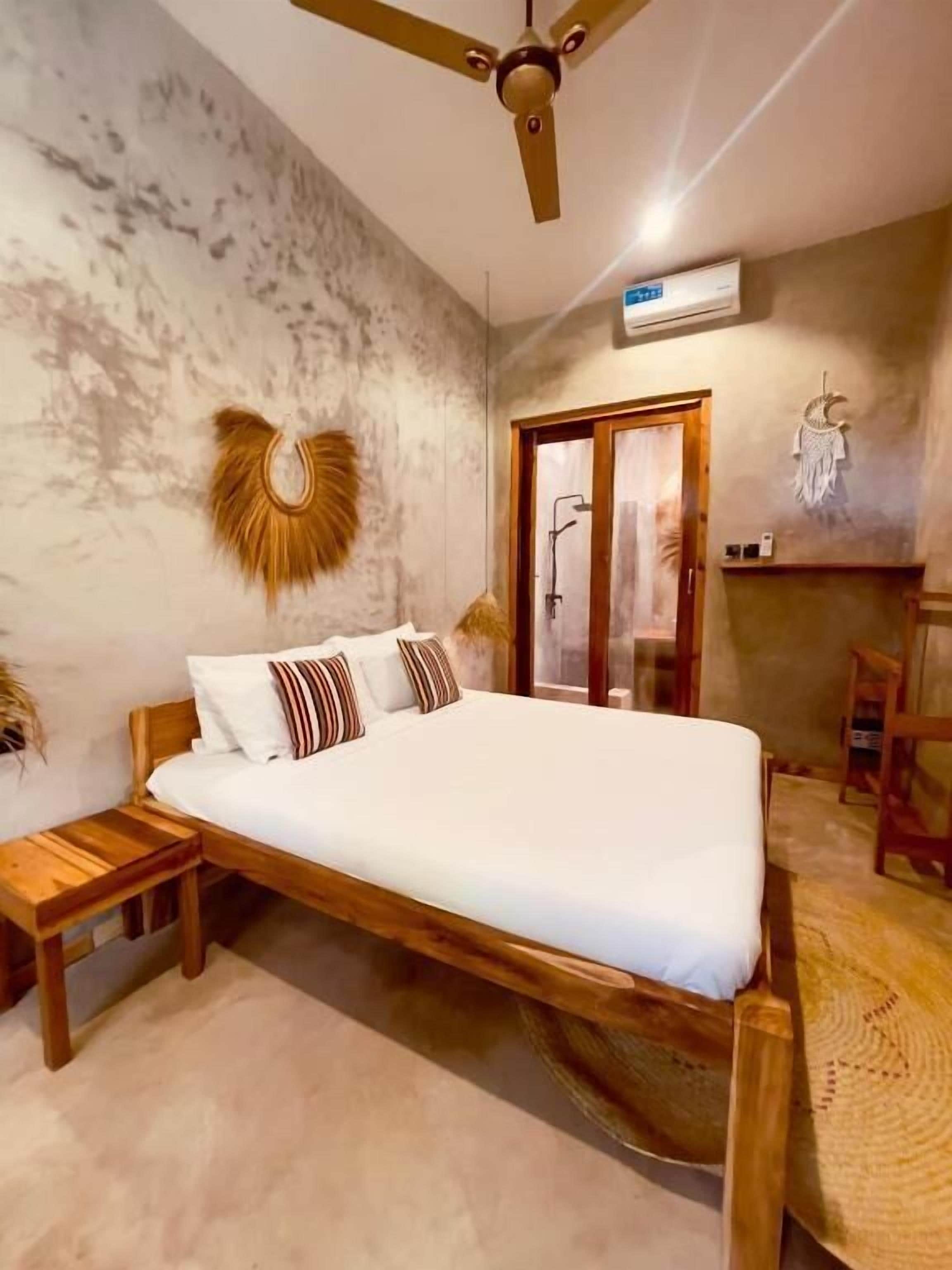 Quarto com cama de madeira, ventilador de teto, ar condicionado fixado na parede e porta com chuveiro.