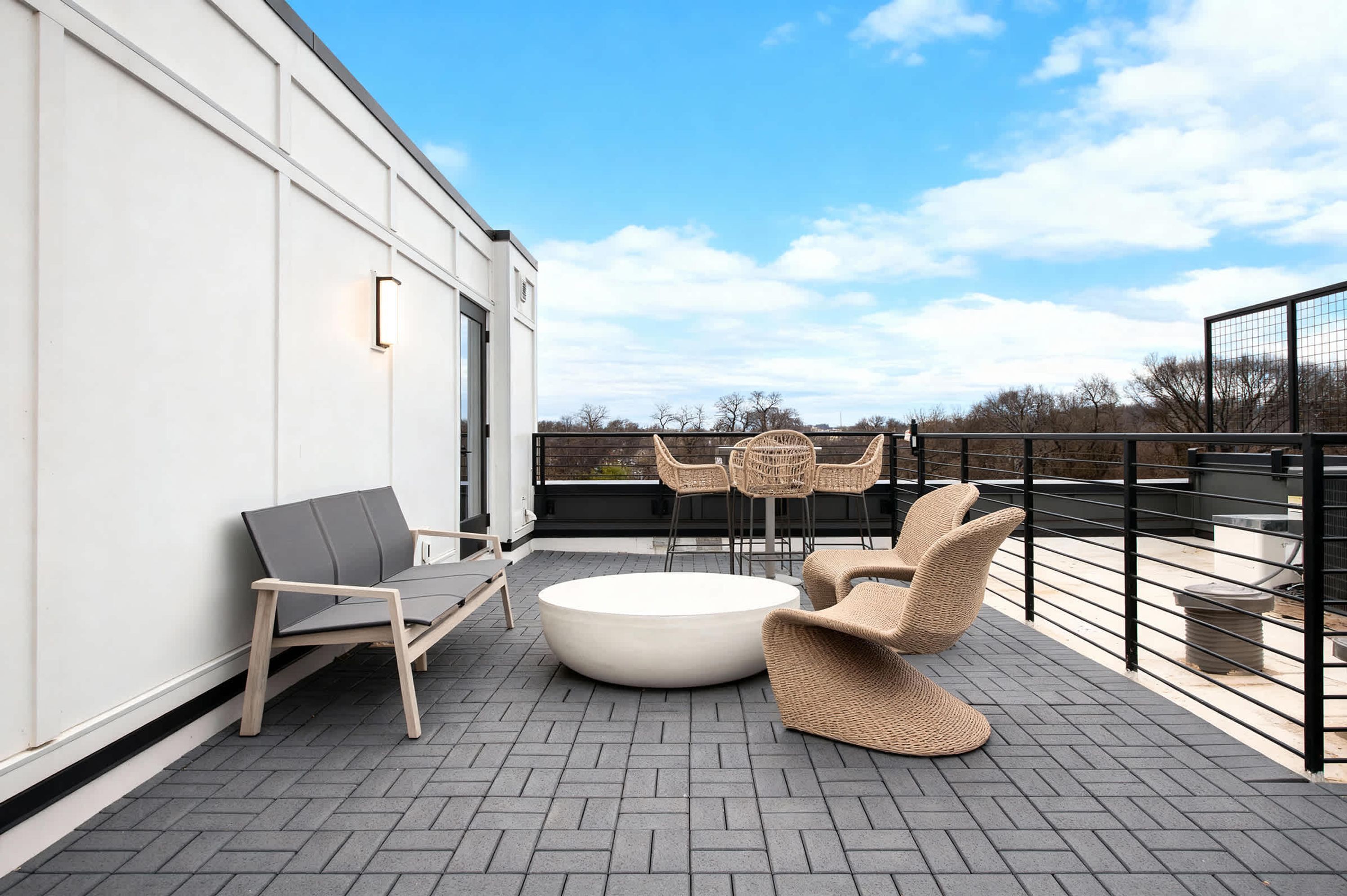 Terraço no telhado com área de estar moderna ao ar livre, incluindo um sofá e cadeiras de vime, e uma mesa branca redonda.