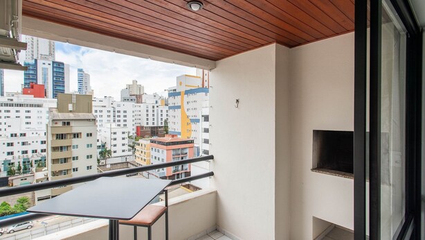 Varanda com mesa e cadeiras, uma televisão e vista para a cidade.