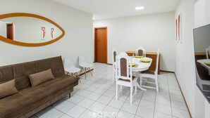 Uma sala de estar com um sofá marrom, cadeiras brancas, uma mesa de jantar e uma televisão.