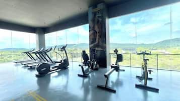 Uma academia com máquinas de cardio, equipamentos de musculação e amplas janelas com vista para o exterior.