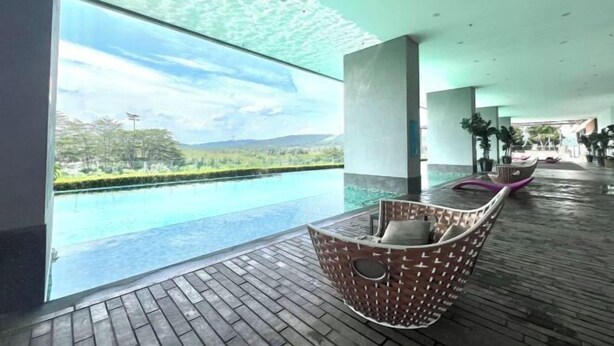Um hall de hotel moderno com uma grande janela de vidro que dá para uma piscina e vegetação exuberante.