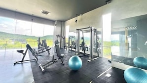Academia com equipamentos de ginástica, janelas amplas e vista para o exterior.