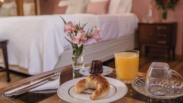 Disposição para o pequeno-almoço com croissants, um copo de sumo de laranja e uma chávena de vidro transparente sobre uma mesa.