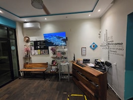 Uma área de recepção com balcão, computador e televisão na parede exibindo uma vista urbana.