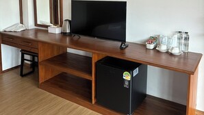 Uma secretária de madeira com uma televisão, um frigorífico pequeno, um espelho e alguns produtos de higiene pessoal.