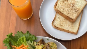 Prato de café da manhã com ovos, salsichas, bacon, batatas, tomates e torradas, acompanhado de um copo de suco de laranja.