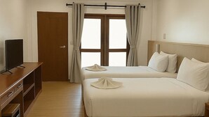 Quarto de hotel com teto de madeira, uma cama grande com lençóis brancos, uma TV sobre uma escrivaninha de madeira e uma janela com cortinas.