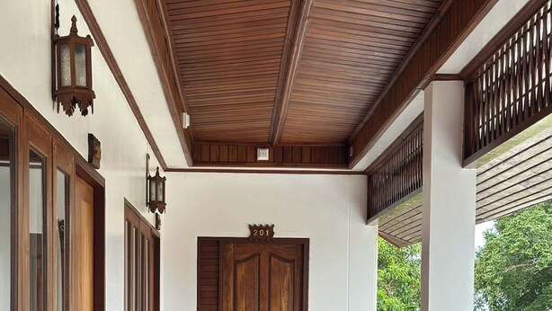 Corredor com portas de madeira, placa indicando o número 201 e uma área de refeições com cadeiras e mesa.