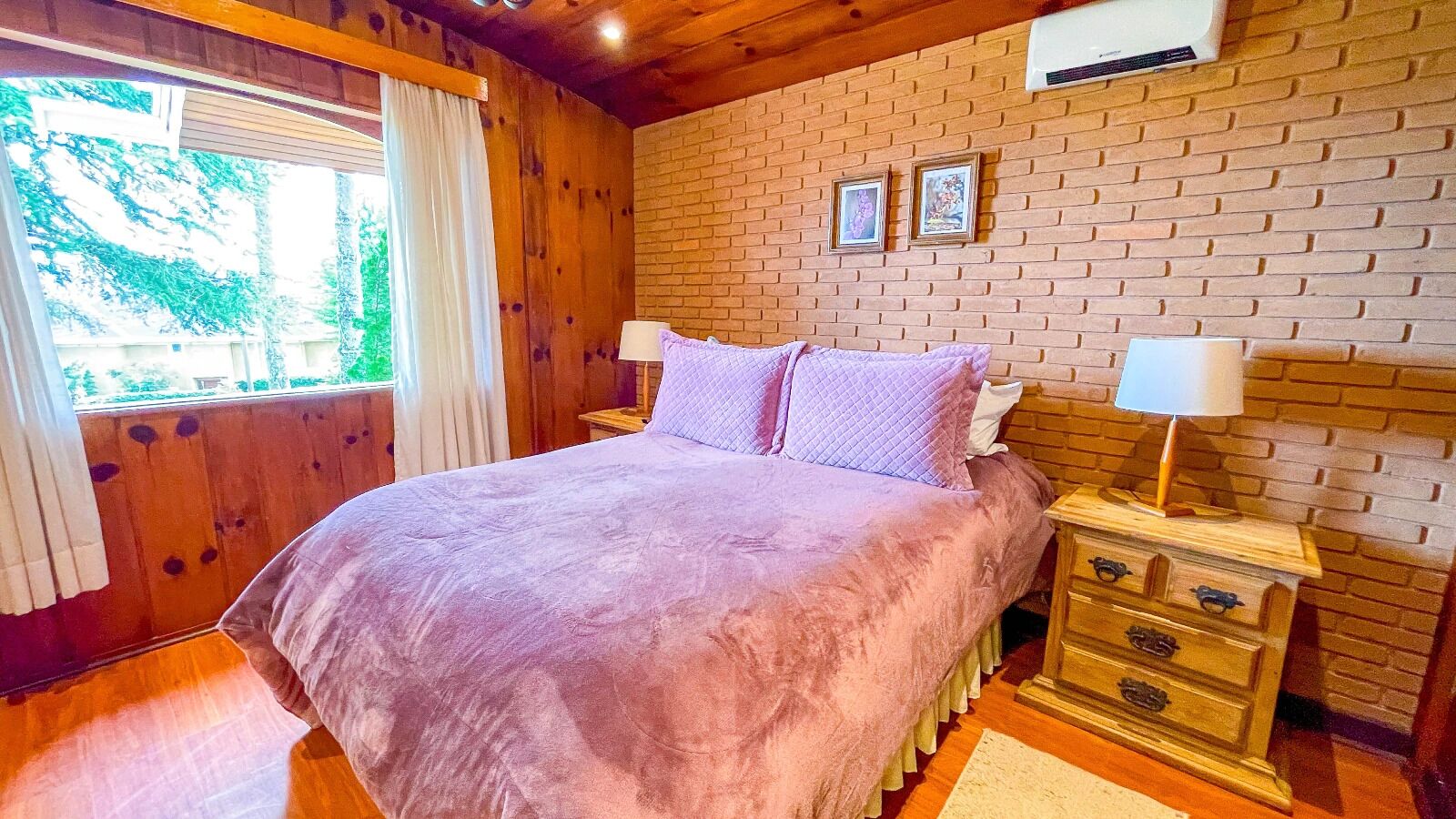 Quarto de cabana de madeira com cama, mesas de cabeceira e uma parede de tijolos.
