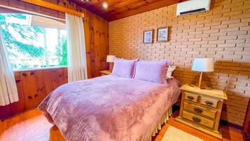 Quarto de cabana de madeira com cama, mesas de cabeceira e uma parede de tijolos.