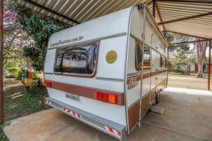 Uma caravana estacionada com área de estacionamento coberta, placa de identificação visível e endereço de site na parte traseira.