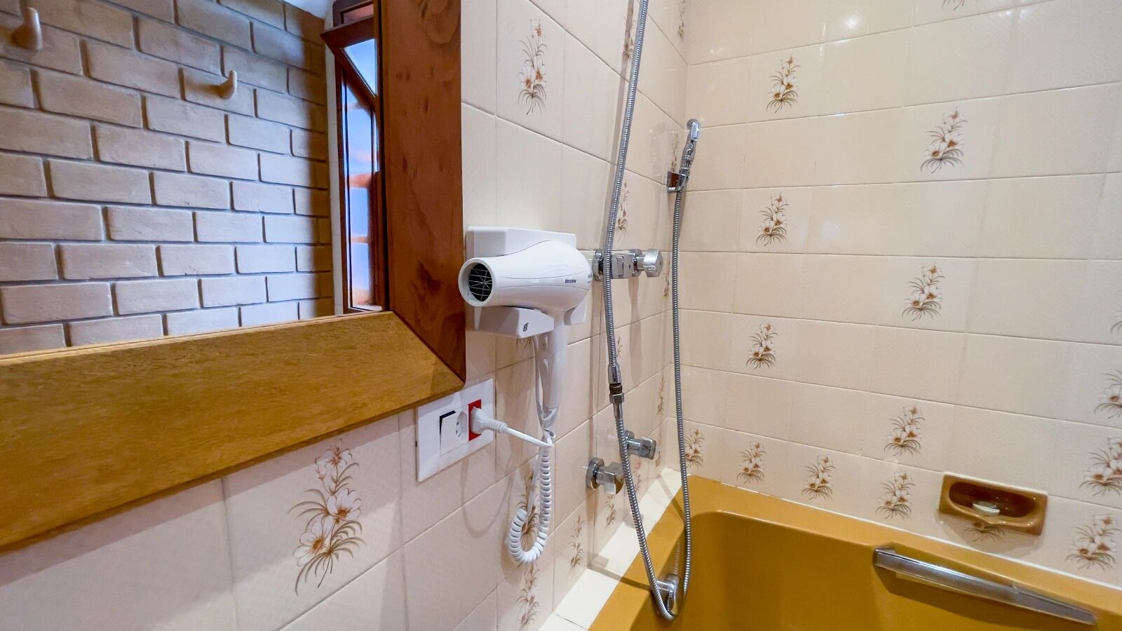 Casa de banho com parede de tijolo, bancada de madeira, secador de cabelo branco, chuveiro com mangueira e banheira amarela.