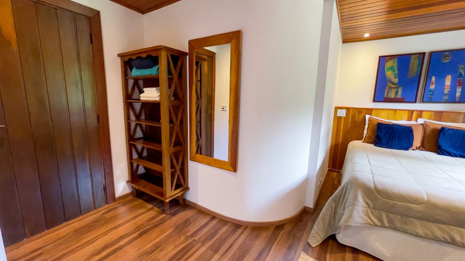 Quarto com guarda-roupa de madeira, cama com cobertura bege e teto de madeira.