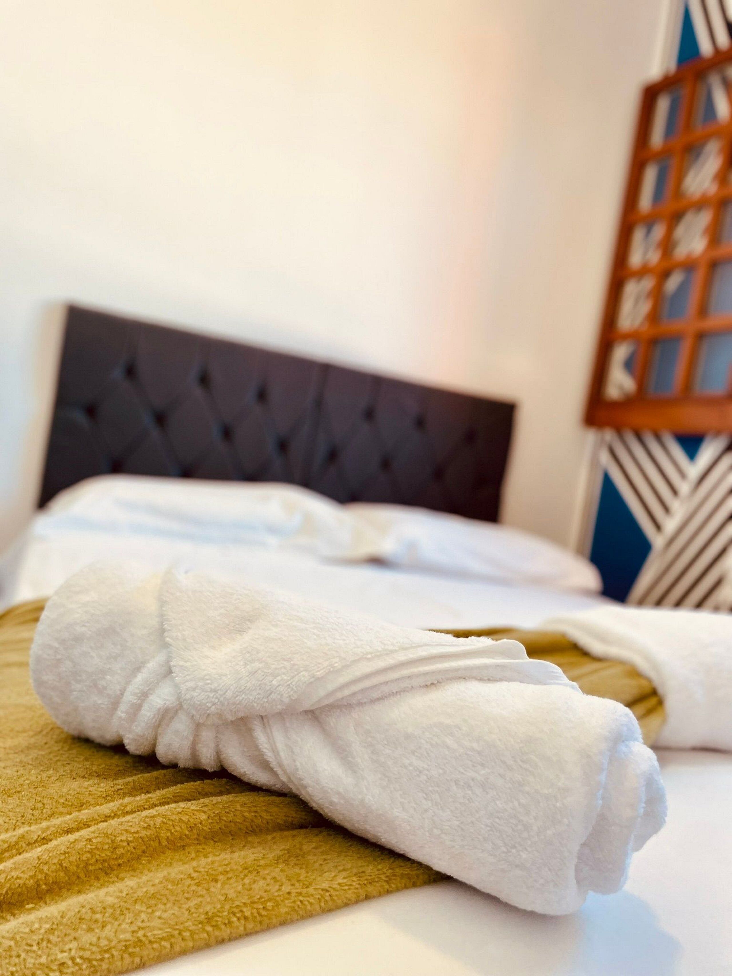 Cama bem arrumada com uma toalha branca dobrada sobre um cobertor verde.