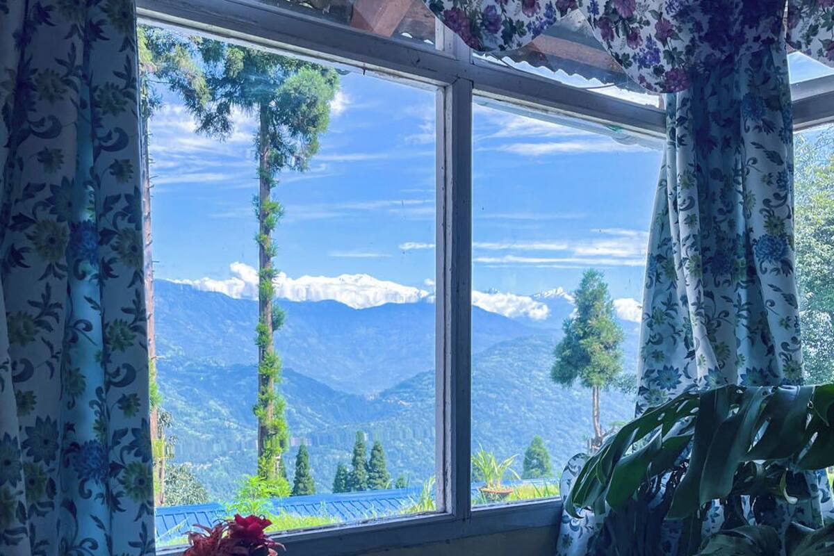 Um quarto com uma janela grande, um laptop sobre a mesa e um vaso com flores.