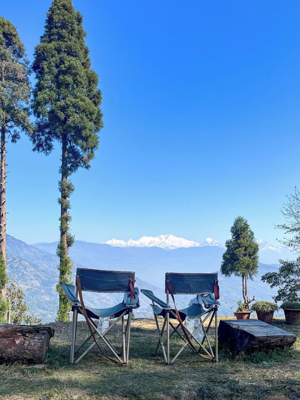 Duas cadeiras dobráveis voltadas para uma vista de montanhas com picos nevados ao longe.