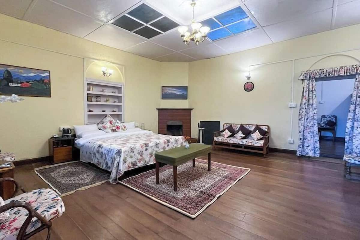 Um quarto com cama, sofá, mesa pequena, lareira, ventoinha no teto e janela com cortinas.