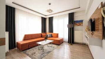 Uma sala de estar moderna com um sofá seccional, uma mesa de centro, um tapete, uma luminária pendente e uma TV de tela plana fixada na parede.