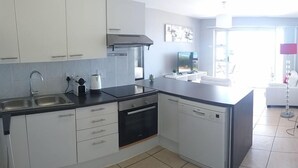 Uma cozinha moderna com armários brancos, bancada preta, lava-louças e fogão.