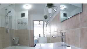 Casa de banho moderna com chuveiro em cabine de vidro, espelho grande e lavatório branco.