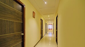 Um corredor de hotel com portas de madeira, piso de azulejos e acesso a um quarto com cortina vermelha.