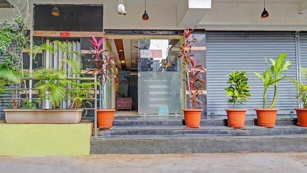 Fachada com vasos de plantas, uma porta com persiana fechada e um aviso indicando elevador.