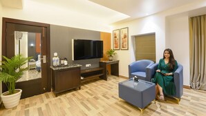 Quarto de hotel moderno com televisão de tela plana, sofá, mesa de centro e um vaso com planta.