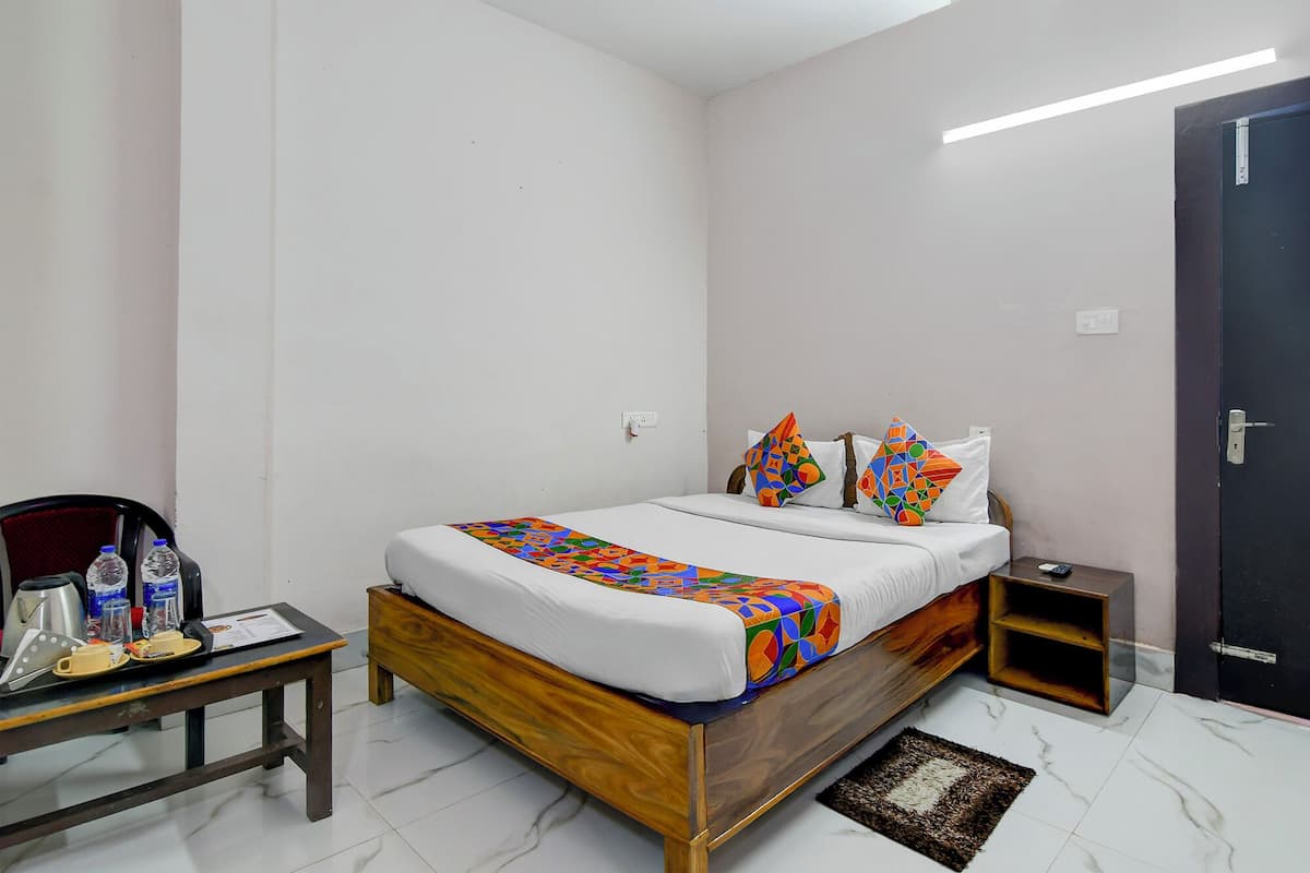 Quarto com cama de madeira, roupa de cama branca, almofadas coloridas, uma pequena mesa de cabeceira, uma cadeira e uma cafeteira.