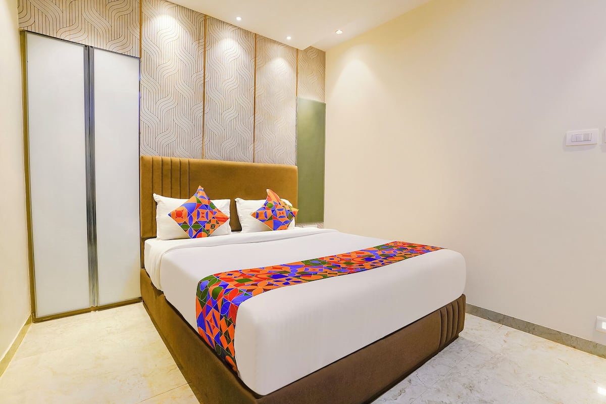 Quarto de hotel com uma cama grande, cabeceira de madeira e parede estampada.